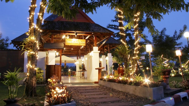 Um gazebo de madeira com luzes de corda, rodeado por plantas em vasos e um caminho que leva à entrada.