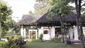 Um edifício em estilo tradicional com telhado de telhas, cercado por vegetação exuberante e um gramado bem cuidado.
