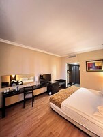 Quarto de hotel com cama, escrivaninha, cadeira e um espelho grande.