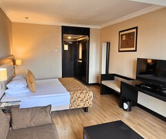 Quarto de hotel com cama, escrivaninha, televisão, cadeira e luminária.