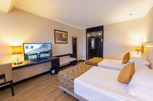 Quarto de hotel com duas camas, uma mesa de escritório com um computador, uma televisão e um quadro na parede.