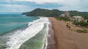 Uma praia com vista clara do oceano, areal arenoso e uma colina arborizada ao fundo.