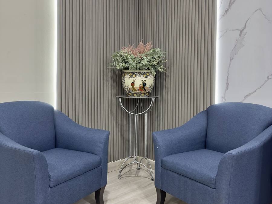 Quarto com duas poltronas azuis, uma planta decorativa em suporte e parede listrada com padrão de mármore.