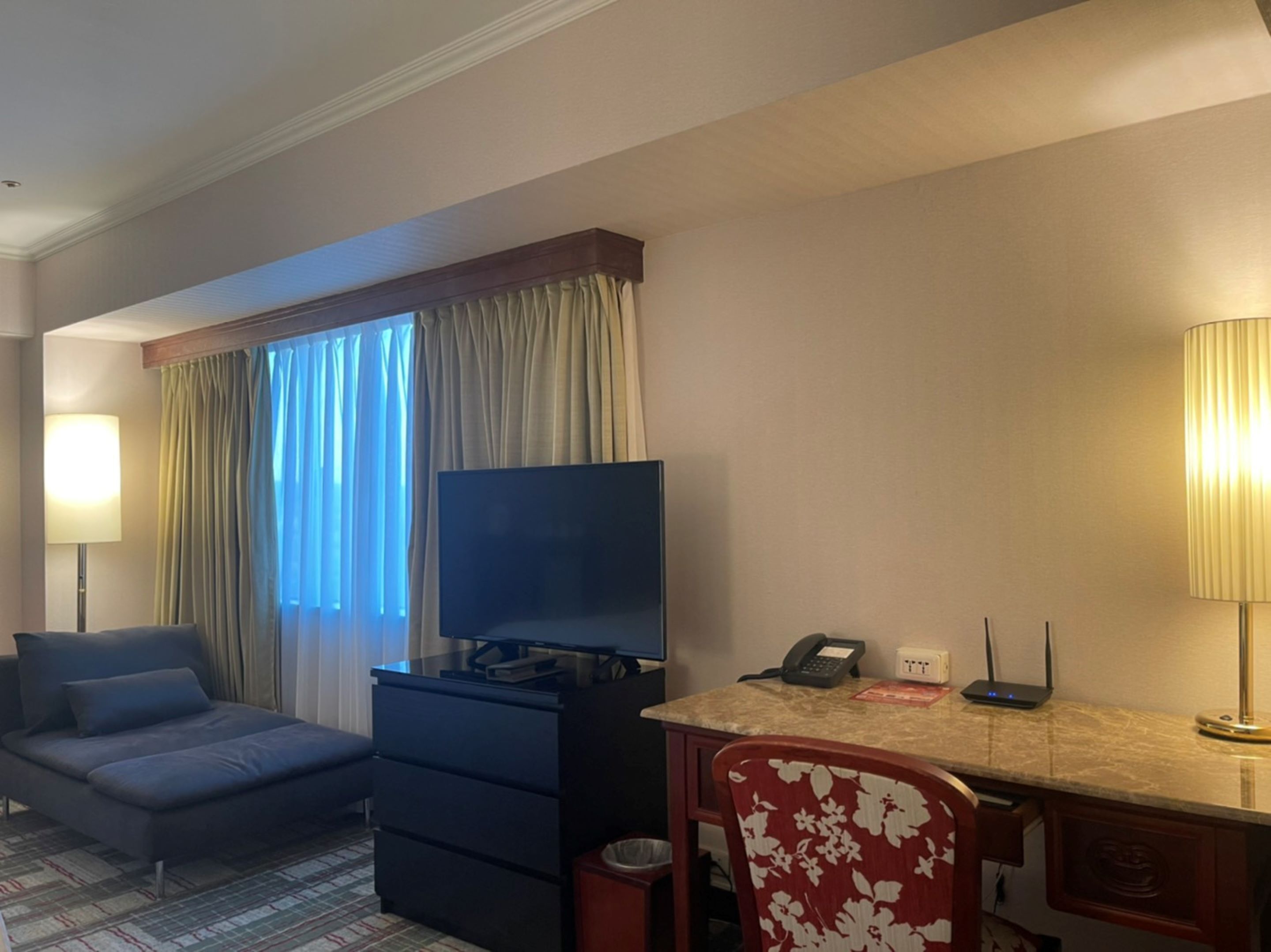 Quarto de hotel com sofá, televisão, escrivaninha com luminária e telefone.