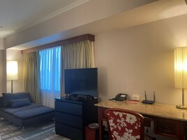 Quarto de hotel com sofá, televisão, escrivaninha com luminária e telefone.
