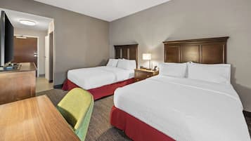 Quarto de hotel com duas camas, uma mesa, uma cadeira, uma televisão e uma luminária.