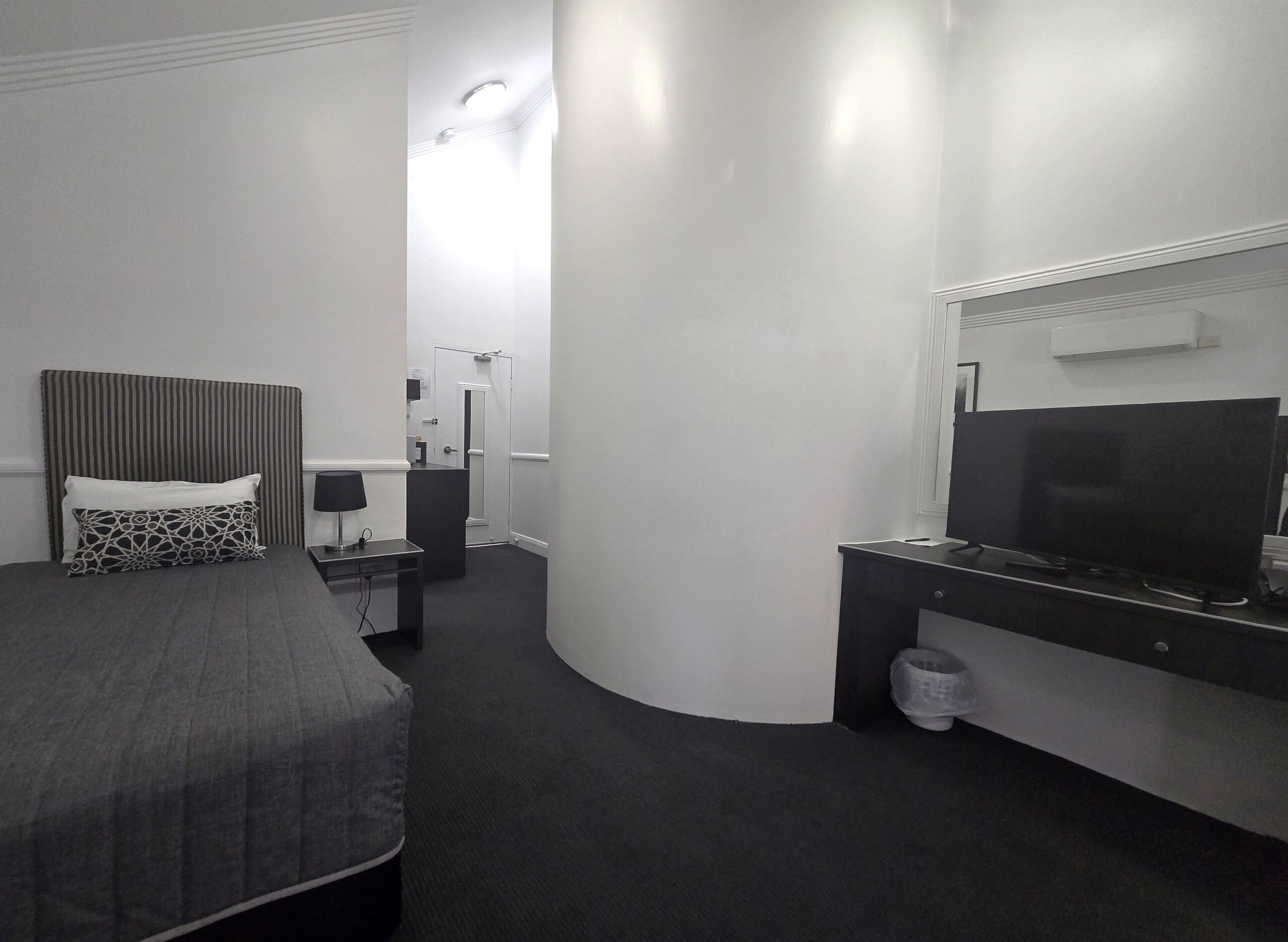 Quarto de hotel com cama, escrivaninha, televisão e banheiro.