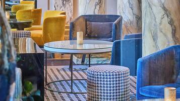 Um saguão com paredes de mármore, assentos em amarelo e azul, e um candelabro.