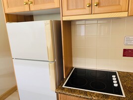 Uma cozinha com geladeira branca, fogão por indução preto e armários de madeira.