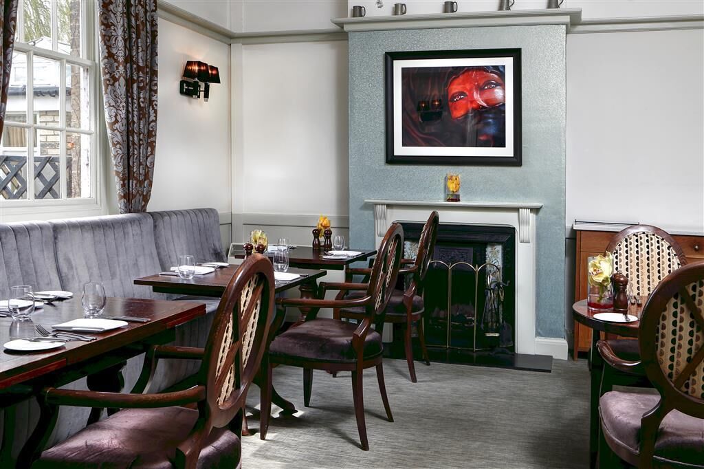 Uma sala de jantar com lareira, cadeiras de madeira, um banco e uma obra de arte emoldurada sobre a lareira.