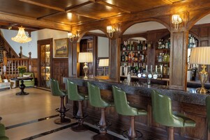 Uma área de bar com banquetas de madeira, um balcão e diversos tipos de garrafas.