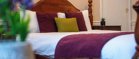 Uma cama bem arrumada com cabeceira de madeira, uma mesinha de cabeceira e um vaso com planta.