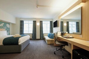 Quarto de hotel com cama, escrivaninha, cadeira, televisão e janela com cortinas.