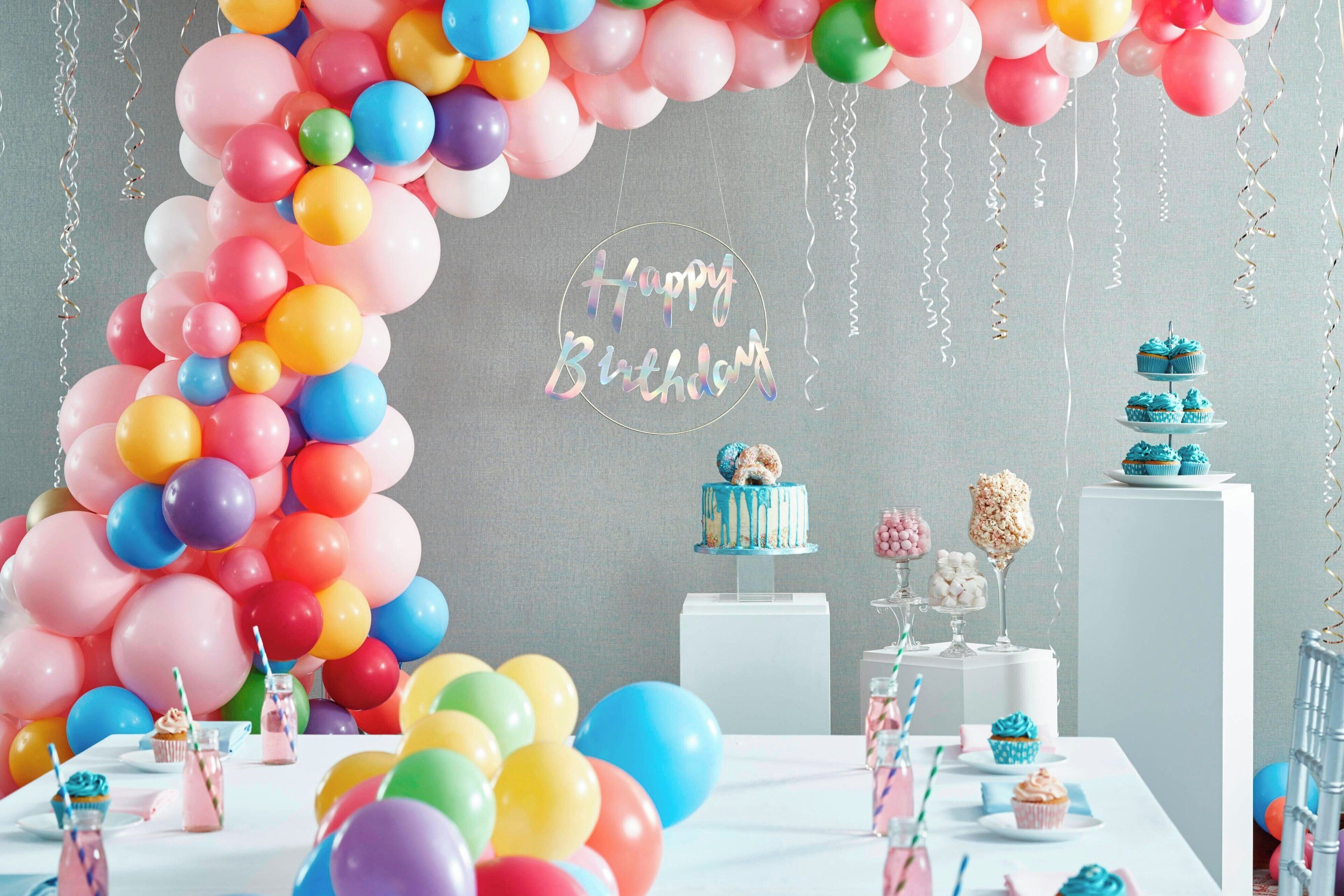 Decoração de festa de aniversário com balões, bolo, cupcakes e um letreiro com a mensagem 'Happy Birthday'.