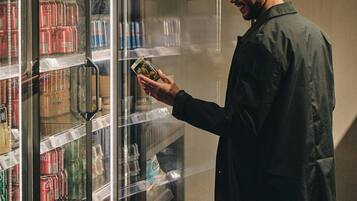 Uma pessoa vestindo uma camisa escura em frente a uma vitrine refrigerada com diversos alimentos.