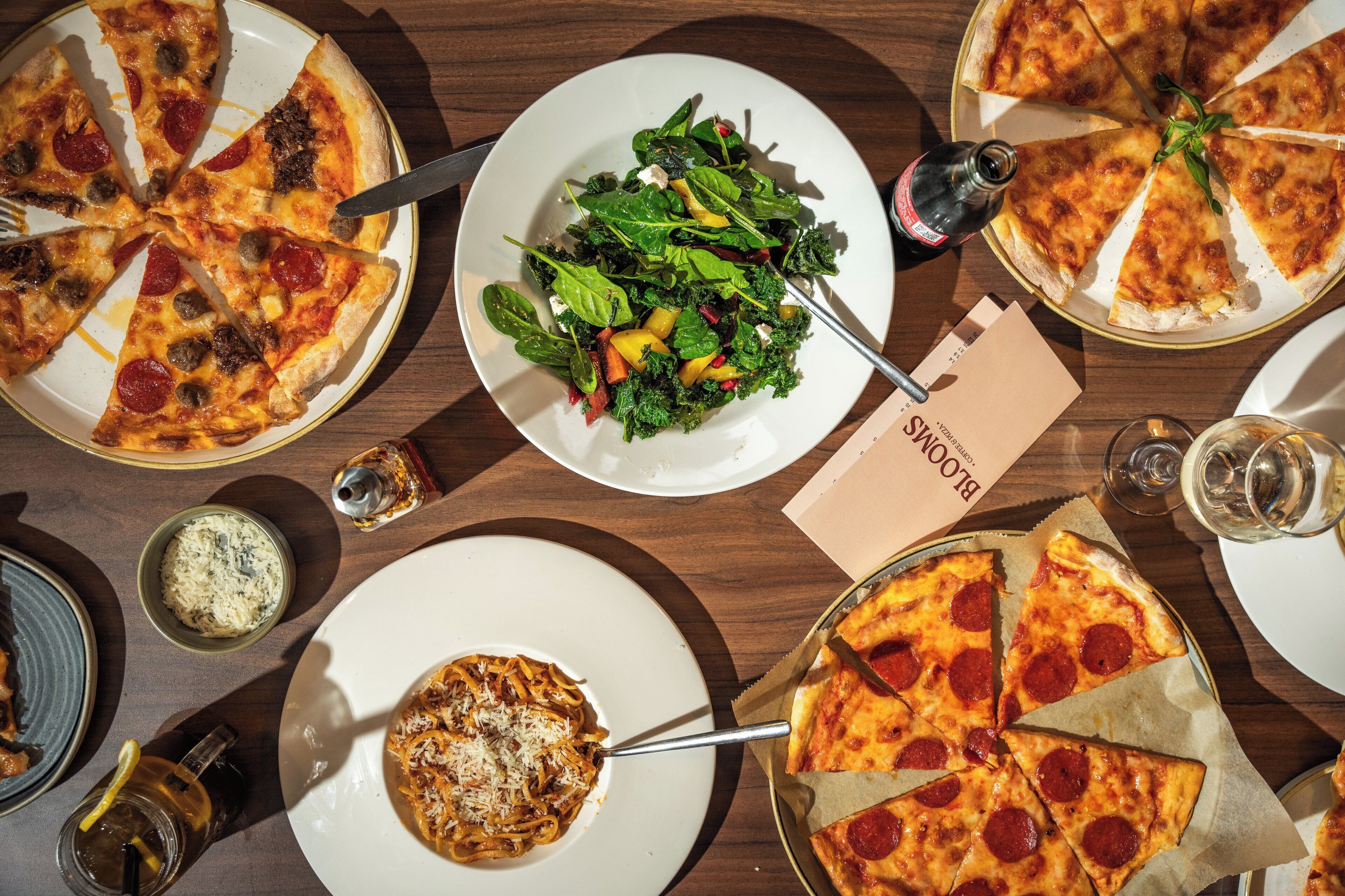 Uma mesa de jantar com diversos pratos, incluindo pizza, massa e uma salada.
