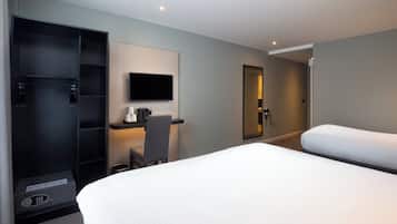 Quarto de hotel com cama, escrivaninha com cadeira, televisão, guarda-roupa e espelho.