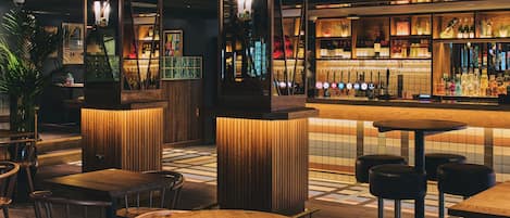 Uma área de bar com mesas e banquetas de madeira, balcão com garrafas e copos, e piso estampado.