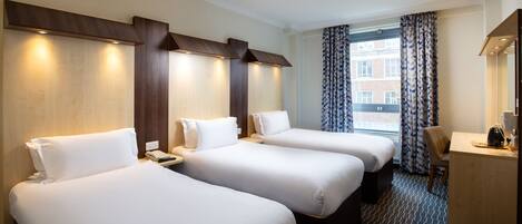 Quarto de hotel com três camas de solteiro, uma escrivaninha e uma cadeira.