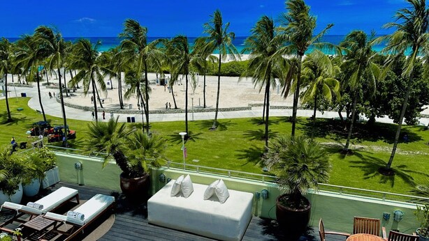 Uma varanda com vista para a praia, palmeiras e cadeiras de lounge.