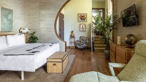 Quarto com uma cama grande, uma cômoda, uma cadeira, uma mesa pequena e um vaso com planta.