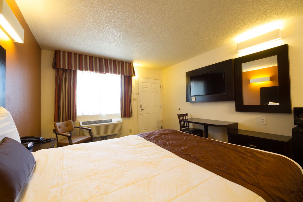 Quarto de hotel com uma cama grande, uma escrivaninha, uma cadeira, uma televisão e uma janela com cortinas.