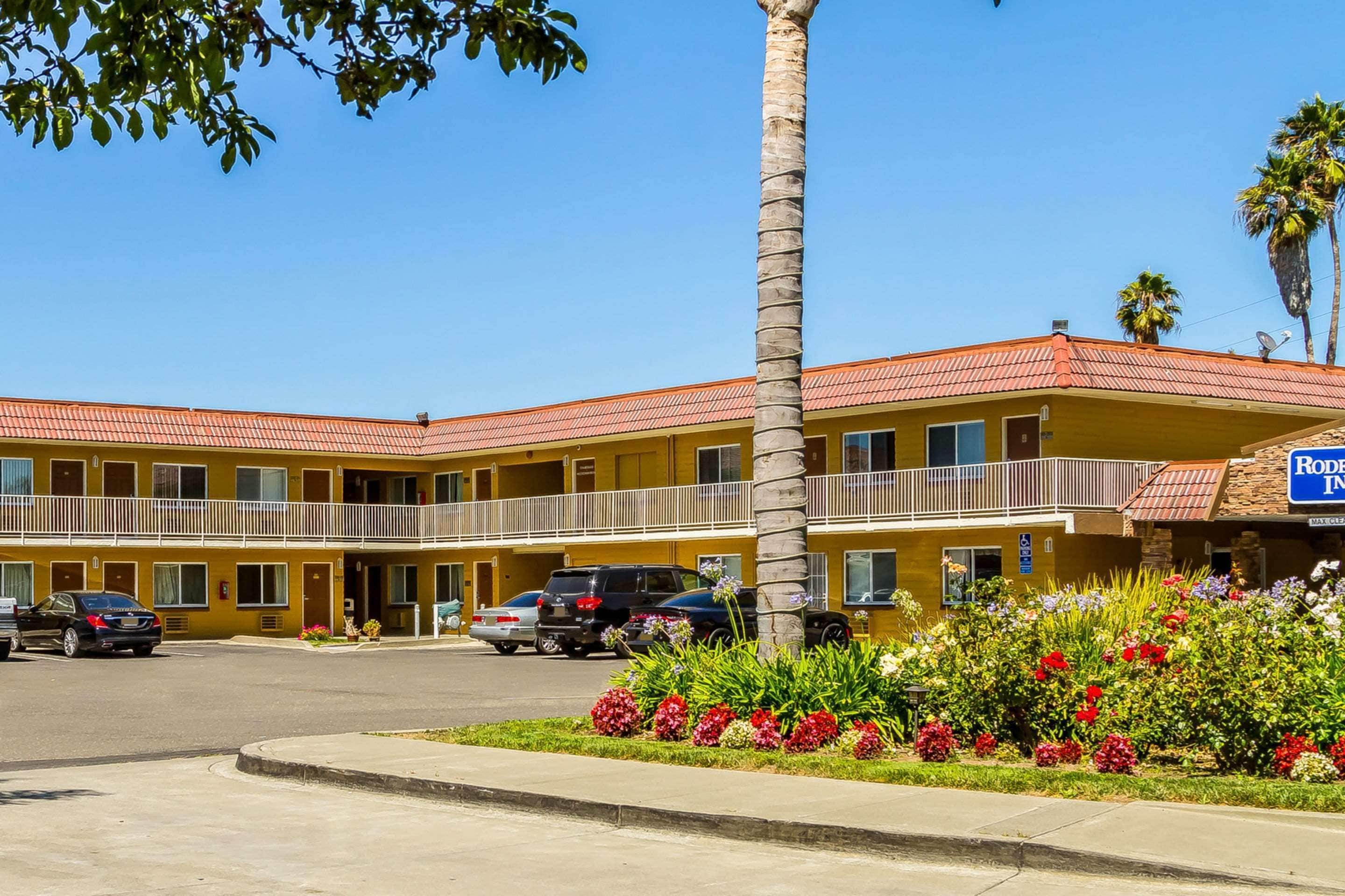 Um motel com telhado de telhas vermelhas, várias varandas e um estacionamento com diversos carros.