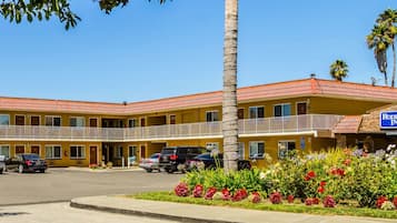 Um motel com telhado de telhas vermelhas, várias varandas e um estacionamento com diversos carros.