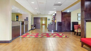 Um hall de hotel com piso de madeira, um balcão de recepção, uma área de espera com cadeiras e um corredor que leva a outra seção.