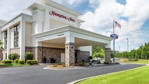 Um hotel Hampton Inn com entrada coberta, fachada de tijolos e uma bandeira americana.