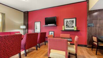 Quarto de hotel com uma parede de destaque vermelha, uma TV de tela plana montada acima de uma mesa e cadeiras com padrão em vermelho e bege.