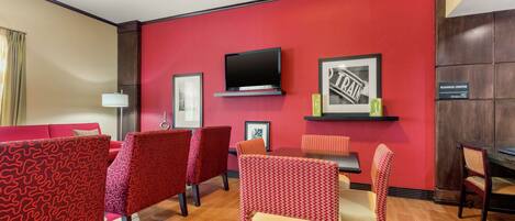 Quarto de hotel com uma parede de destaque vermelha, uma TV de tela plana montada acima de uma mesa e cadeiras com padrão em vermelho e bege.