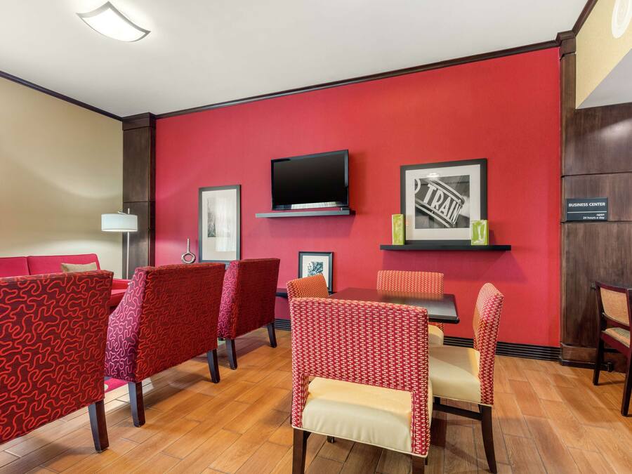 Quarto de hotel com uma parede de destaque vermelha, uma TV de tela plana montada acima de uma mesa e cadeiras com padrão em vermelho e bege.