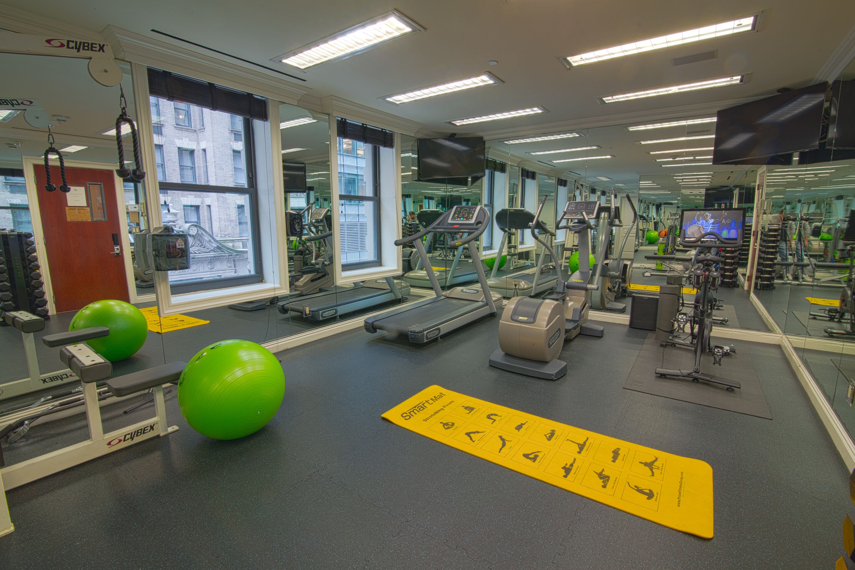 Academia com equipamentos de ginástica, espelhos e um tapete amarelo de instrução.