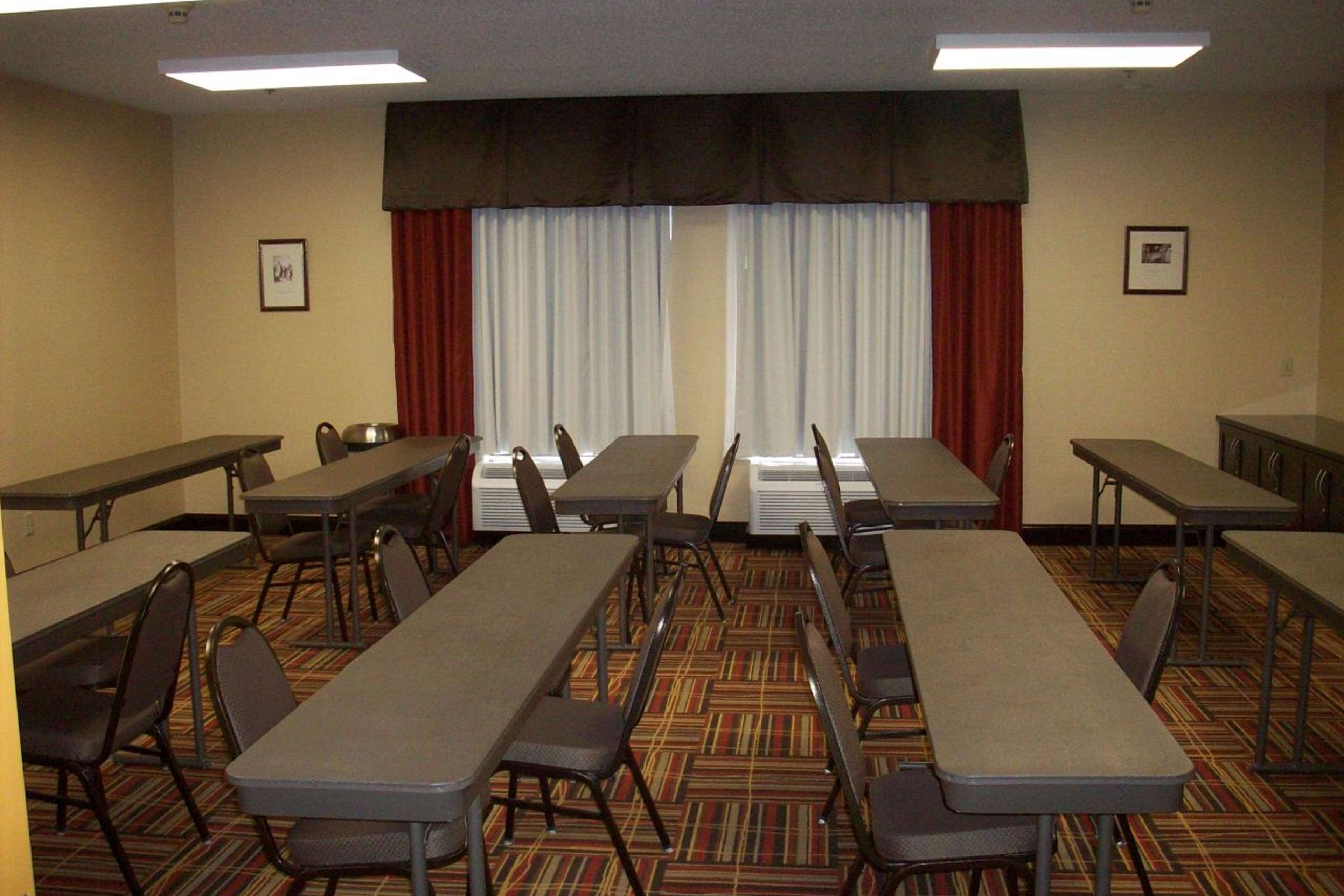 Uma sala de conferências com várias mesas e cadeiras, um tapete estampado e uma grande janela com cortinas.