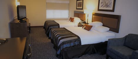 Quarto de hotel com duas camas, uma escrivaninha com televisão, uma cadeira e uma janela com persianas.