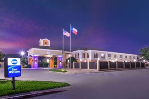 Um hotel Best Western com uma entrada ampla, as bandeiras americana e do Texas, e uma fachada bem iluminada.