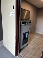 A vending machine labeled "ICE CUBE DISPENSER" in a hallway with wooden flooring and beige walls.