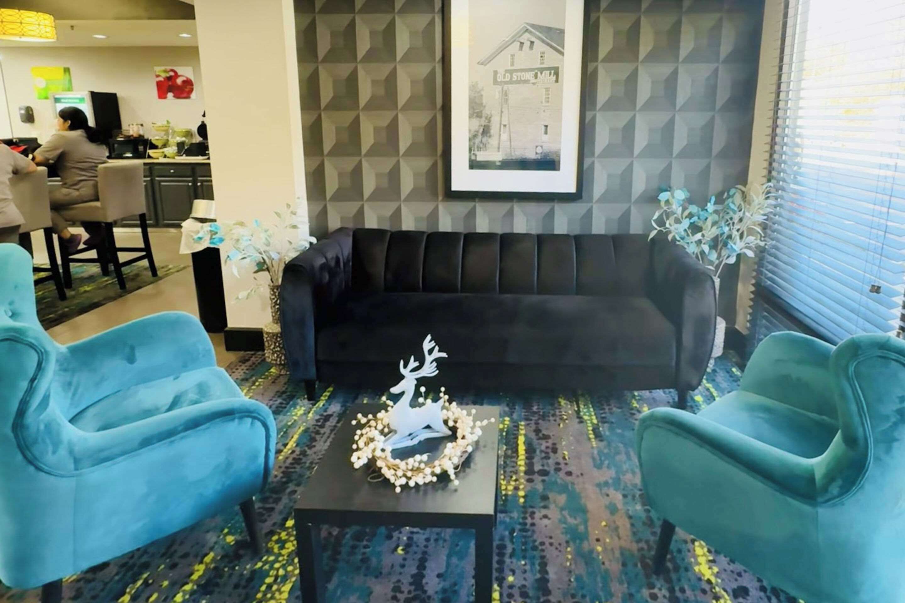 Um lobby moderno com um sofá preto, duas poltronas azuis e uma peça central decorativa para a mesa.