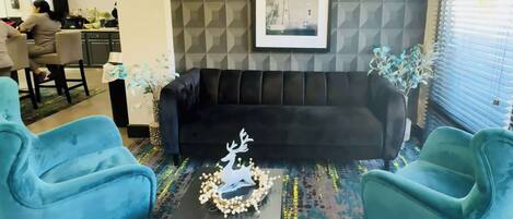 Um lobby moderno com um sofá preto, duas poltronas azuis e uma peça central decorativa para a mesa.