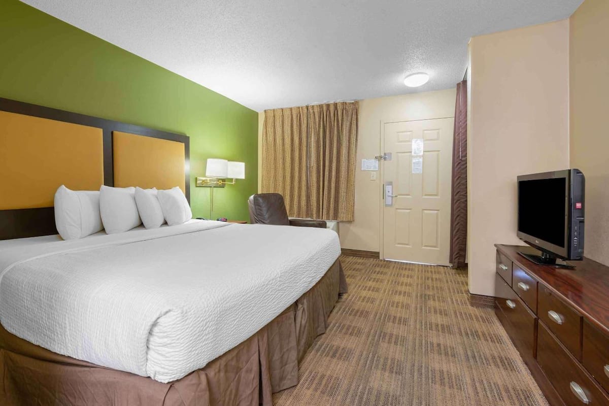 Quarto de hotel com uma cama grande, televisão, escrivaninha e cadeira.