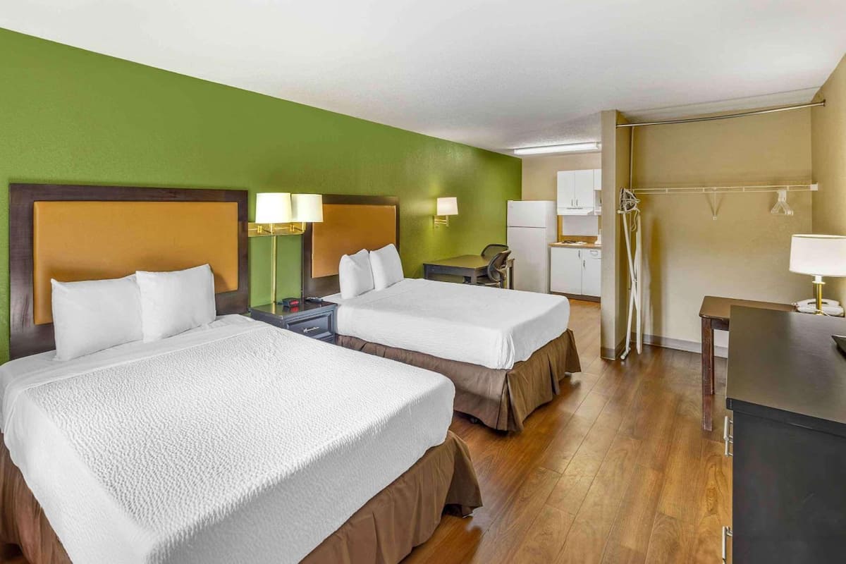 Quarto de hotel com duas camas, uma secretária, uma cadeira e um guarda-roupa.