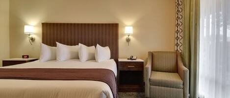Quarto de hotel com uma cama grande, duas mesas de cabeceira, uma cadeira e uma janela com cortinas translúcidas.