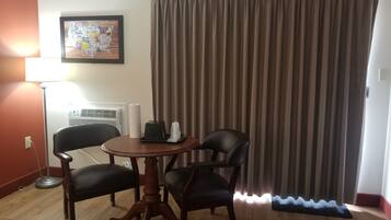 Quarto com mesa de madeira redonda, duas cadeiras pretas, um mapa emoldurado na parede, um ar condicionado e uma cortina.
