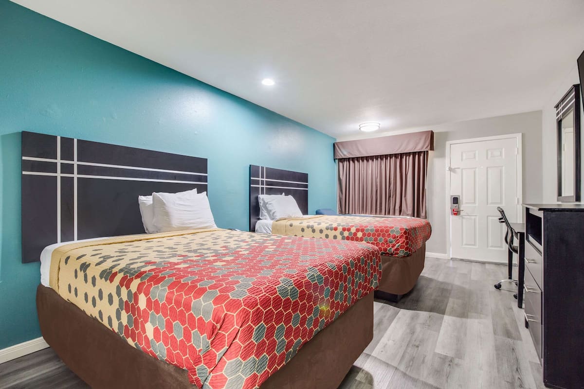 Quarto de hotel com duas camas, paredes verde-água e piso de madeira.