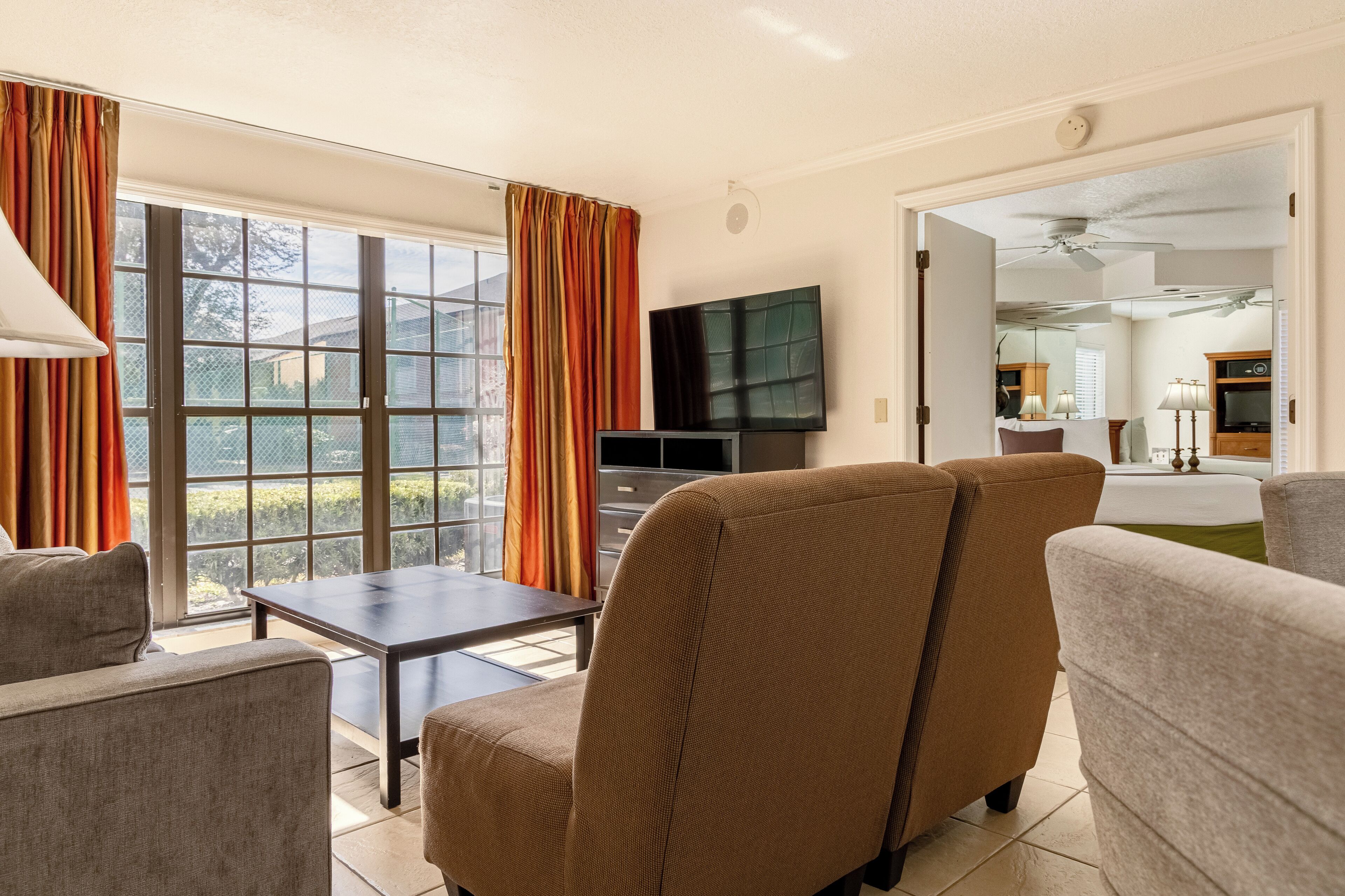 Sala de estar com sofá, mesa e televisão. Possui uma porta de vidro deslizante com cortinas.