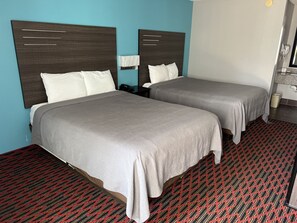 Quarto de hotel com duas camas, uma mesa de cabeceira, abajur e espelho de banheiro.
