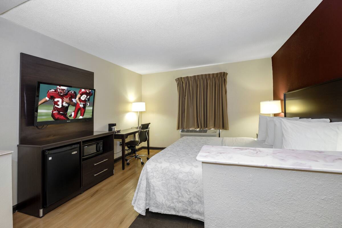 Quarto de hotel com cama, escrivaninha, televisão e minibar.