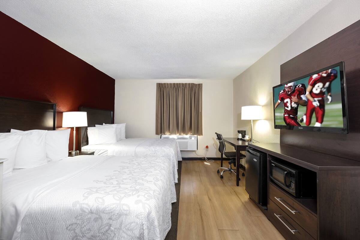 Quarto de hotel com duas camas, uma escrivaninha com cadeira, televisão e micro-ondas.