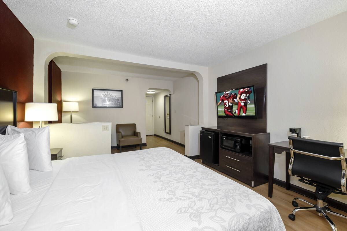 Quarto de hotel com uma cama grande, uma escrivaninha com computador, uma televisão e uma cadeira.